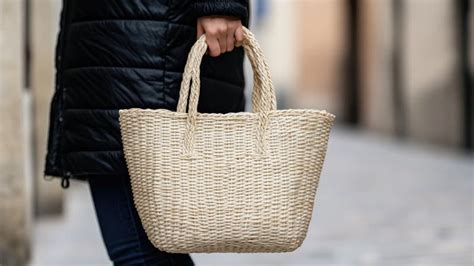 A Close Up Captures A Woman In A Floral Dress And Straw Bag Walking