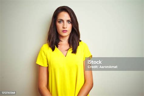 얼굴에 심각한 표정과 흰색 고립 된 배경 위에 서 노란색 티셔츠를 입고 젊은 아름다운 여성 카메라를 보는 간단하고 자연스러운 T 셔츠에 대한 스톡 사진 및 기타 이미지