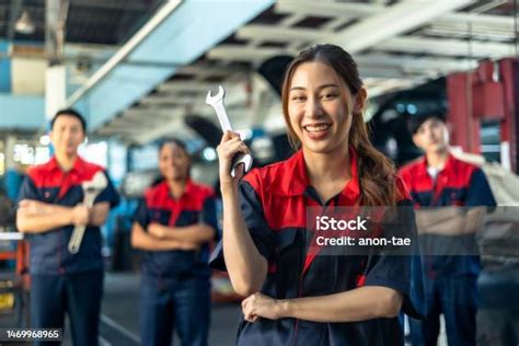 차고의 리프터에서 차량 상태를 확인하는 엔지니어 팀 제복을 입은 젊은 자동차 정비사가 카메라를 바라보며 웃으며 차를 살펴보고