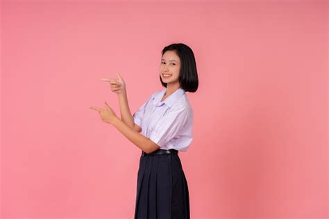 아시아의 10대 여학생이 옆으로 돌아서서 미소를 지으며 손가락으로 무언가를 가리킨다 유명 학교 및 과외 기관의 교육 발표자 분홍색 배경 스튜디오에서 사진 찍기 가상현실에