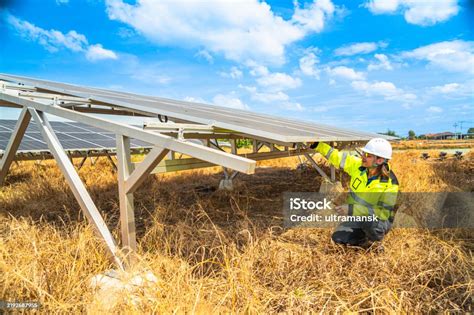 안전 장비를 착용한 기술자가 맑고 푸른 하늘과 흩어져 있는 흰 구름을 배경으로 풀이 무성한 태양광 발전소에서 전동 드릴을 사용하여 태양 전지판을 유지 보수하고 있습니다 2