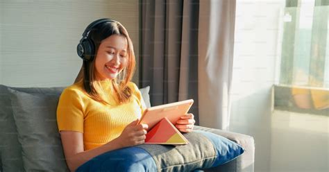 소파에 앉아 헤드폰으로 음악을 들으며 아파트에서 비즈니스 프로젝트를 위한 디지털 태블릿 작업을 하고 있는 아시아 여성 여성 프리랜서 작업 계획 또는 집에서 온라인 메시지를