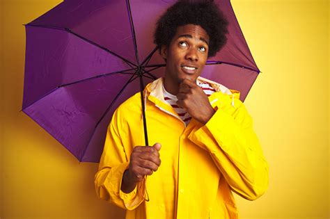 비옷과 우산을 입고 고립 된 노란색 배경 심각한 얼굴에 서있는 아프로 미국 남자 질문에 대해 생각 매우 혼란 스러운 생각 개념에 대한 스톡 사진 및 기타 이미지 Istock