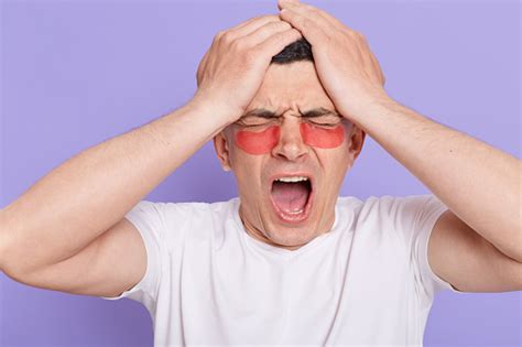 슬픈 분노의 감정을 표현하는 눈 아래에 보습 패치를 착용하고 큰 소리로 비명을 지르는 절망적 인 젊은 성인 남성은 머리와 눈을