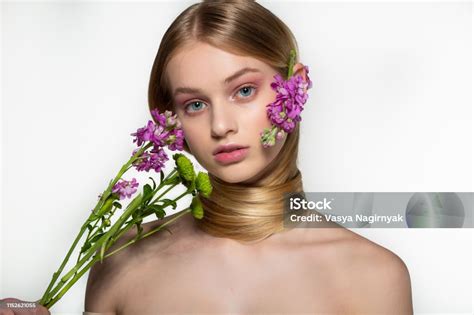 파란 눈을 가진 아름 다운 젊은 여성 모델 어깨에 꽃과 완벽 한 피부 그녀의 목은 머리에 싸여 여자는 카메라를 보고 있다 회색