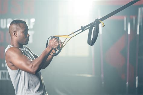 흑인 아프리카 운동 선수 남자는 Trx가 경기장의 강철 빔에 고정되어 근육을 유지하고 강도를 구축하고 피트니스 클럽이나 체육관에서 유연성을 높이기 위해 팔을 똑바로 내밀고