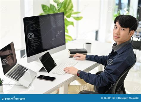 professional asian male programmer sits at his office desk smiling at looking at the camera
