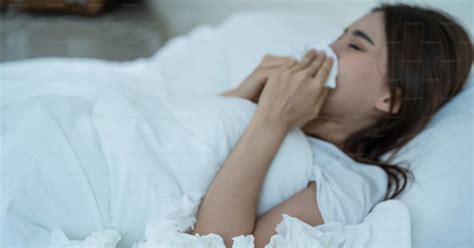 잠옷을 입은 아시아 아픈 소녀는 침대에서 재채기를 하는 밤에 잠에서 깨어난다 기분이 좋지 않고 알레르기로 고통받는 매력적인