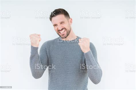 잘생긴 젊은이 매우 행복 하 고 흥분 무기와 우승자 제스처를 하 고 격리 된 배경 위에 캐주얼 스웨터를 입고 웃 고 성공을 위한 비명 축 하 개념입니다 긍정적인 감정 표현에