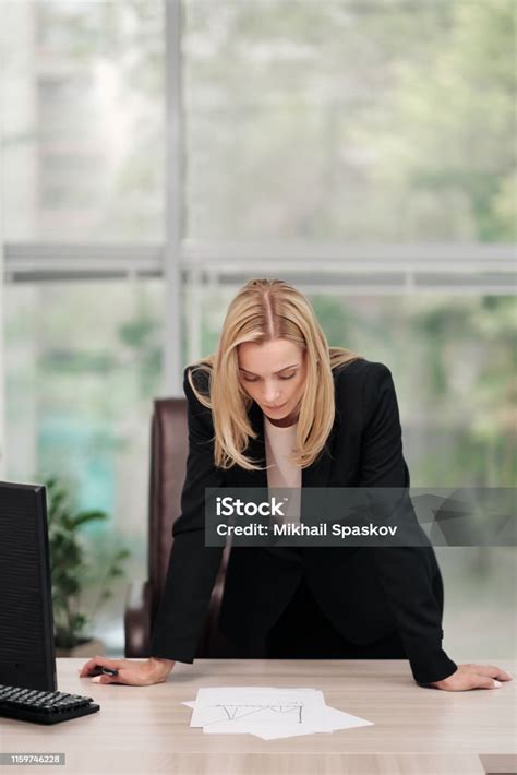 젊은 매력적인 백인 금발의 여자 에 검정 비즈니스 정장 에 앉아 책상 에 밝은 사무실 종이 문서를 공부하고 카메라를 보고 미소짓습니다 감독에 대한 스톡 사진 및 기타 이미지