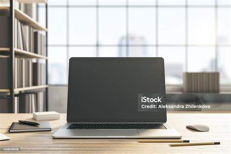현대 노트북 빈 검은 색 모니터의 정면보기는 도시 전망 배경이있는 흐릿한 창에 사무용 도구가있는 밝은 나무 테이블에 텍스트 또는