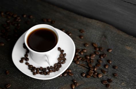 나무 테이블 배경에 구운 커피 콩커피 컵 나무 테이블에 흩어져 있는 커피 콩이 있는 검은 색 코프 잔 신선한 커피 콩 갈색에