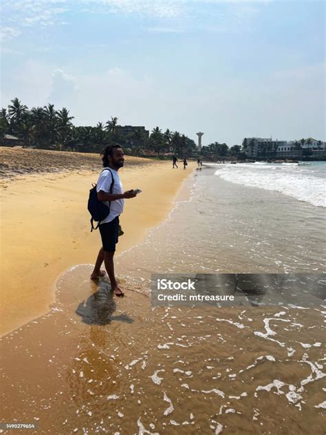 바닷가에 맨발로 서 있는 인도 남자의 이미지 마운트 라비니아 해변 스리랑카 콜롬보에서 휴가를 보내고 반바지와 티셔츠를 입고 비치 슈즈를 들고 배낭을 어깨에 메고 바다를