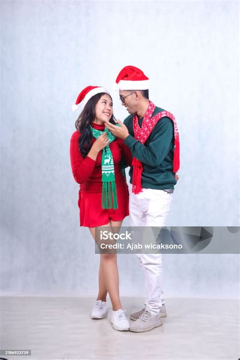 전신 산타 모자와 따뜻한 옷을 입고 서 있는 두 명의 행복한 아시아 사람들이 서로를 바라보며 크리스마스와 새해를 축하하며 흰색 배경에 고립되어 있습니다 20 24세에 대한