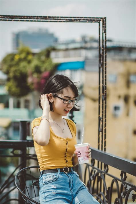 흰색 컵을 들고 검은 선글라스를 착용 한 노란색 탱크 탑을 입은 여자 사진 Unsplash의 무료 의복 이미지