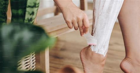 제모 개념 탈모 과정 흰 수건을 쓴 젊은 여성이 다리에 면도 크림을 바르고 녹색 식물이 있는 집 욕실에서 플라스틱 면도기를 들고 있다 스킨 케어 사진