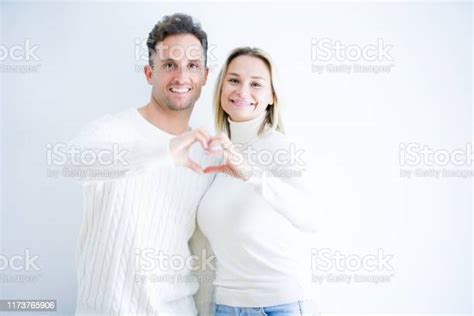 고립 된 흰색 배경 위에 서있는 캐주얼 한 티셔츠를 입은 젊은 아름다운 부부는 손으로 심장 기호와 모양을 보여주는 사랑에 미소 로맨틱 한 개념 2명에 대한 스톡 사진 및