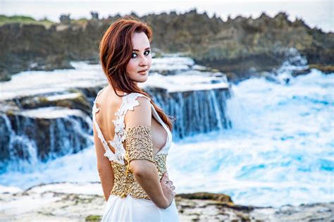 해변에서 흰색과 황금 색 레이스 드레스를 입은 젊은 아름다운 여성 뒤를 돌아보고 바다 바위와 폭포 배경 파스텔 색상 복사 공간 도미니카 공화국에 대한 스톡 사진 및 기타