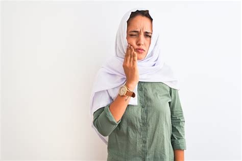 치아에 치통이나 치과 질환으로 인해 고통스러운 표정으로 손을 만지는 고립 된 배경 위에 전통적인 이슬람 히잡을 착용한 젊은 아름다운 아랍 여성 치과 의사 개념 건강관리와