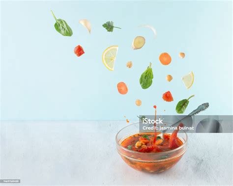 신선한 유기농 식물 기반 재료가 고립 된 파스텔 블루 배경의 유리 그릇에 수프를 튀기는 모로코 병아리 콩 위에 떠 있습니다 건강 식품이나 전통 주방의 최소한의 창조적 개념