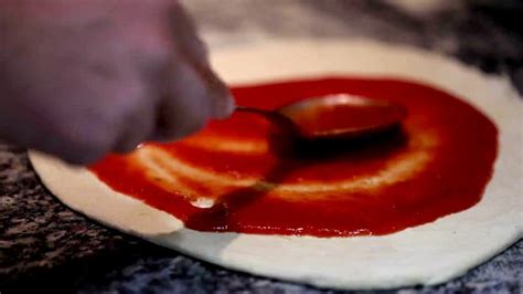 厨师把新鲜的番茄酱涂在生的比萨饼上。