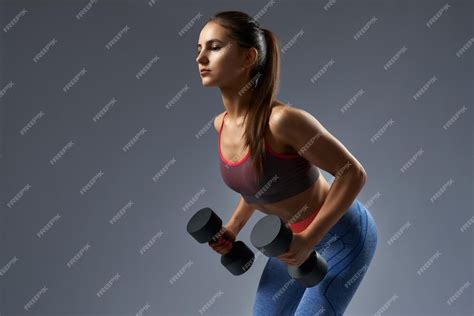 Привлекательная уверенная в себе фитнес девушка накачивает мышцы бицепса Бесплатно Фото