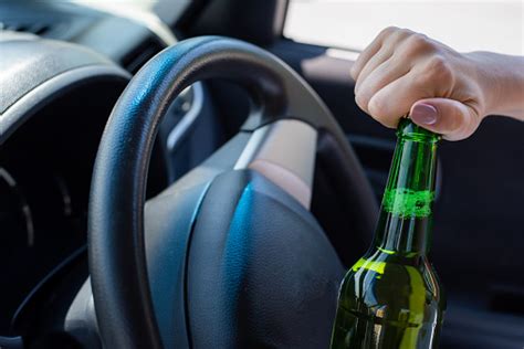 얼굴을 초월한 여성이 차를 운전하는 동안 맥주 한 병을 엽니다 운전 중 법을 위반하고 술을 마시는 고속도로에 대한 스톡 사진 및