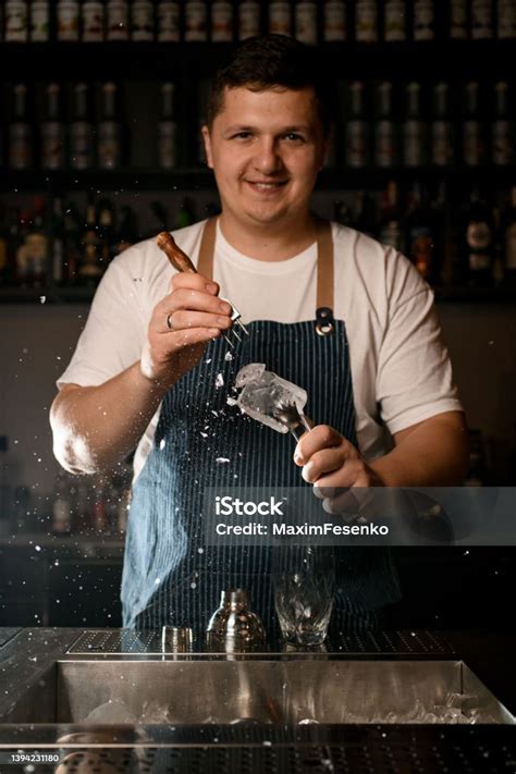 어린 미소 바텐더는 집게로 얼음 조각을 들고 커팅 나이프로 쪼개어 놓습니다 요리사에 대한 스톡 사진 및 기타 이미지 요리사 바텐더 요리하기 음식 준비 Istock