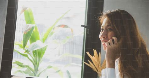 하얀 드레스를 입은 젊은 사업가가 카페의 테이블에 앉아 노트북에 글을 쓰고 있다 스마트폰과 커피 한 잔을 말하는 아시아 여성 커피숍에서 일하는 프리랜서 온라인 학습을