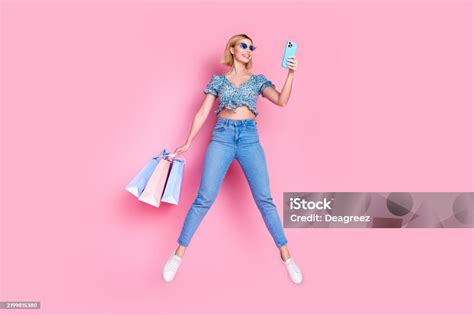 반짝이는 아가씨 옷을 입은 블루 탑 점프 의사 소통 현대 가제트 보유 쇼핑객 고립 핑크 컬러 배경의 전체 길이 사진 Brand Name Smart Phone에 대한 스톡