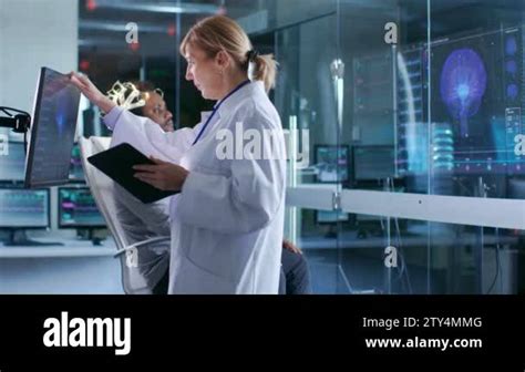 Man Wearing Brainwave Scanning Headset Sits In A Chair While Scientist Uses Touchscreen Display