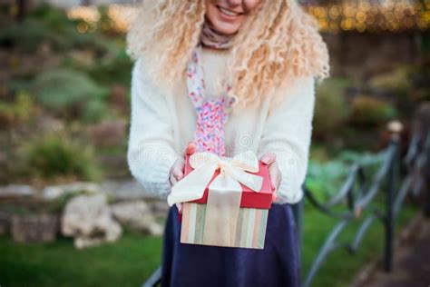 Close Up Focused T Box With Satin Ribbon In The Hands Of Smiling Curly Blond Woman In Warm