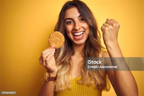 회색 고립 된 배경을 통해 비스킷을 먹는 젊은 아름다운 여성은 자랑스럽게 비명을 지르고 승리와 성공을 축하하는 매우 흥분 응원 감정 쿠키에 대한 스톡 사진 및 기타 이미지