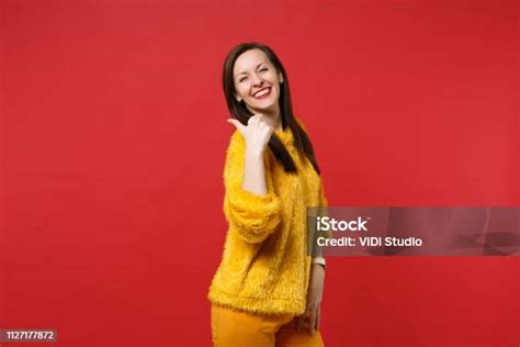 노란 털 스웨터 포인팅 엄지손가락 옆으로 스튜디오에서 밝은 빨간 벽 바탕에 고립 된 젊은 여자를 아름 다운 미소의 초상화 사람들이 진심으 감정 라이프 스타일 개념 복사