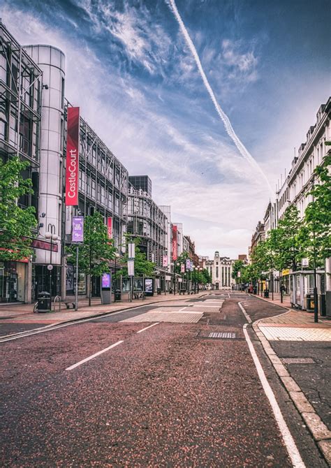 낮에는 푸른 하늘 아래 고층 건물 사이의 회색 콘크리트 도로 사진 Unsplash의 무료 벨파스트 이미지