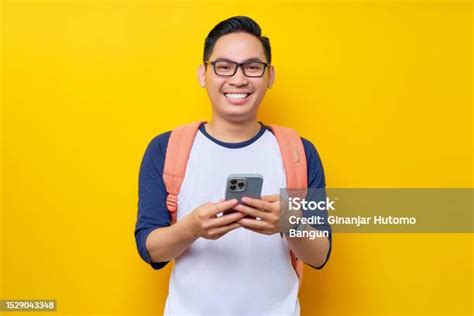 캐주얼 옷 배낭 안경을 쓴 젊은 아시아 남자 학생이 휴대전화를 손에 들고 노란색 배경에 고립되어 있다 고등학교 대학 대학 개념 30 34세에 대한 스톡 사진 및 기타 이미지