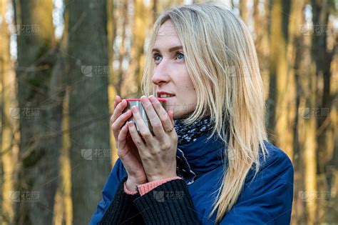 夕阳西下时，在春天的森林里，一位年轻的金发女郎从保温瓶里喝着茶，抬头望着天空。主题旅游。女孩在徒步旅