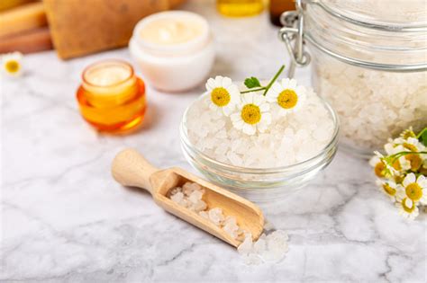 카모마일 스파 카모마일 꽃 수제 비누 에센셜 오일 화장품 병 바디 크림 스크럽 및 바다 소금이 흰색 질감 배경에 있습니다 편안한