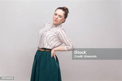 척추 또는 신장 통증 스트라이프 셔츠와 녹색 치마와 수집된 금지 헤어스타일 서와 그녀의 고통 스러운 백을 들고 있는 아름 다운 젊은 여자의 초상화 컷아웃에 대한 스톡 사진