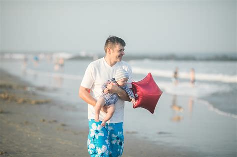 갓난아기 아들과 함께 해변에서 즐거운 시간을 보내는 쾌활한 젊은 아버지 공중에 아이를 던지는 아빠 2명에 대한 스톡 사진 및
