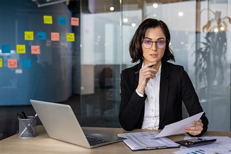 문서를 들고 안경을 쓰고 전략 계획을 세우고 디지털 도구와 다채로운 메모로 둘러싸여 비판적으로 생각하는 현대적인 사무실에서 자신감 넘치는 사업가 개념에 대한 스톡 사진 및