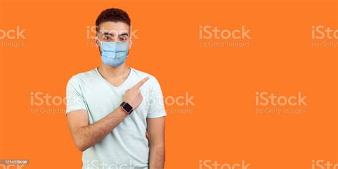 여기 봐 왼쪽을 가리키는 왼쪽 텍스트에 대 한 빈 공간을 가리키는 캐주얼 흰색 티셔츠에 의료 마스크와 갈색 머리 남자의 초상화 광고 보호 마스크에 대한 스톡 사진 및 기타