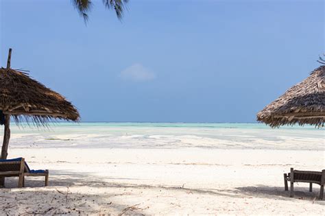 하얀 모래가 있는 해변에 우산이 달린 일광욕용 의자 경치 좋은 바다 풍경 잔지바르 탄자니아 해변 의자 위에 선쉐이드 놀라운 썰물 배경 빈 열대 리조트 파라다이스 자연 넓은