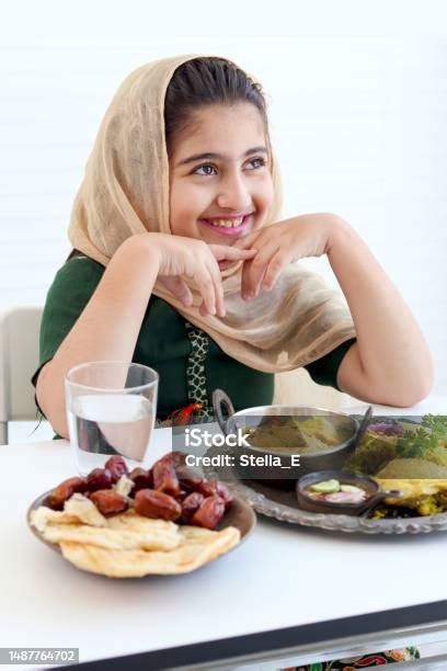 부엌 식탁에 앉아 있는 동안 아름다운 눈을 가진 사랑스러운 웃는 파키스탄 무슬림 소녀 히잡을 쓴 행복한 아이는 전통적인 이슬람 할랄 음식 흰색 배경을 먹는 것을 즐긴다 8