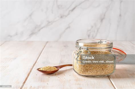 하얀 퀴노아 씨앗을 숟가락에 넣고 흰색 나무 테이블에 상단 유리 항아리를 클립합니다 채식주의 건강한 식습관을위한 생 퀴노아 요리 글루텐 프리 요리를위한 Chenopodium