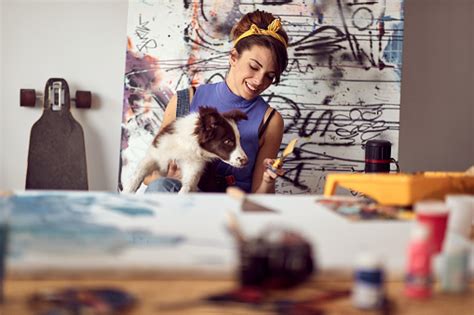 한 젊은 여성 아티스트가 스튜디오에서 새로운 그림을 작업하는 동안 강아지와 놀고 있습니다 예술 회화 우정 스튜디오 20 29세에 대한 스톡 사진 및 기타 이미지 Istock