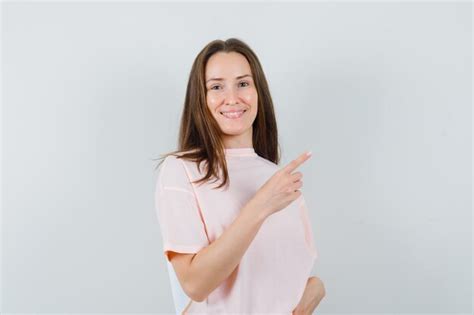 분홍색 티셔츠에 오른쪽 상단 모서리를 가리키고 쾌활한 찾고 젊은 아가씨 무료 사진
