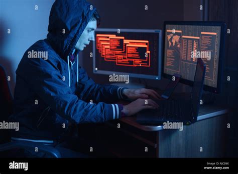 A Male Hacker In A Hood Typing Program Code While Committing A Cybercrime Hacking A System