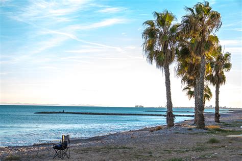 일몰에 야자수가 있는 파라다이스 해변 풍경 지중해 Chilches 발렌시아 스페인 해안에 외로운 테이블과 의자 휴가에서 평화 평온 휴식을 취하십시오 0명에 대한 스톡 사진