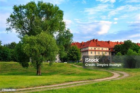 아름다운 잔디밭을 지나 커다란 녹색 나무를 지나 붉은 기와 지붕의 건물로 이어지는 비포장 도로 흰 구름이 있는 푸른 하늘 0명에 대한 스톡 사진 및 기타 이미지 Istock